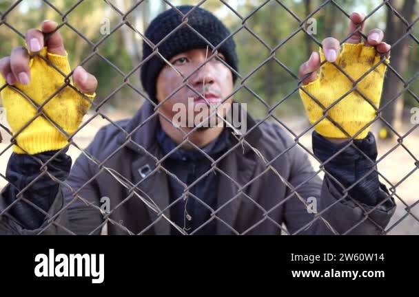 footage of a man standing by the mesh fence and his hands holding on to ...