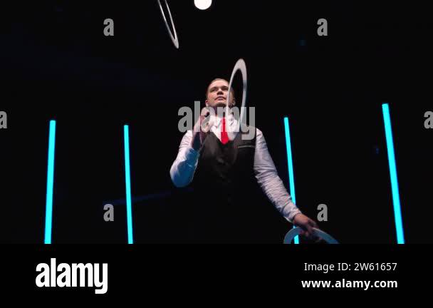 Camera rotates around professional male juggler juggling white rings ...