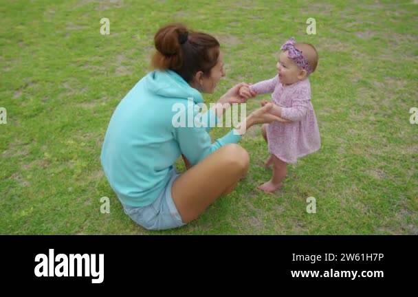 baby takes first steps in grass. mom walks with dauther in nature kid ...