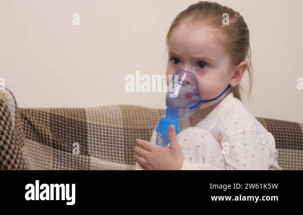 A cute baby in a mask is breathing through an inhaler. Home inhalation ...