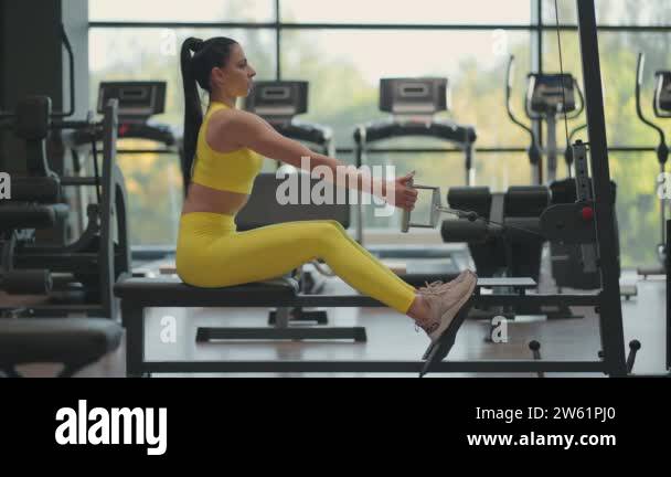 Hispanic Woman Does Exercises On The Rowing Machine A Girl Sits Behind