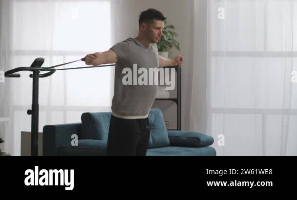 sportsman is training with rubber bands, tensing muscles of arms, back ...