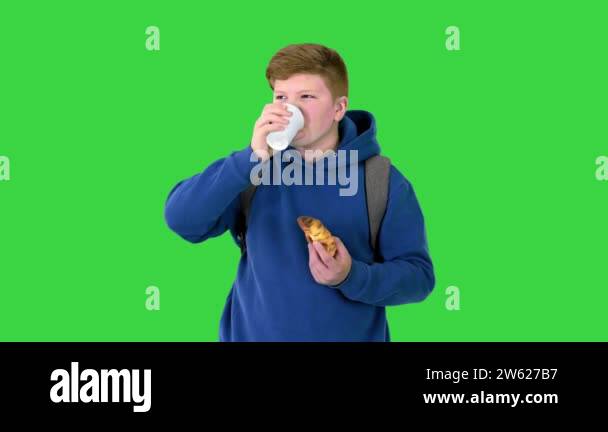 Schoolboy having a croissant and drinking a soft drink on a Green ...