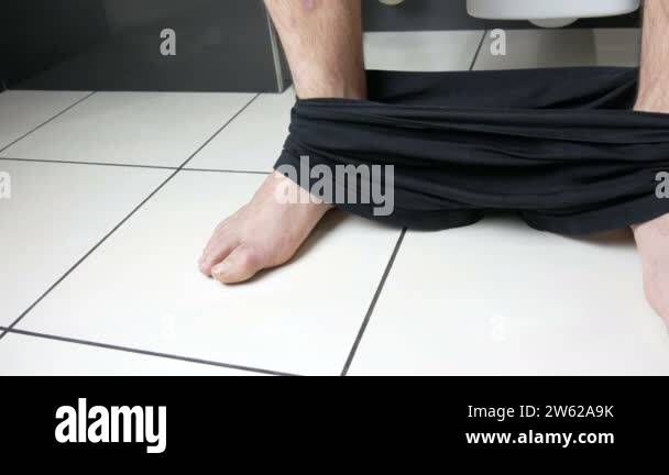 Legs of a man sitting on the toilet in the bathroom. Defecation process ...