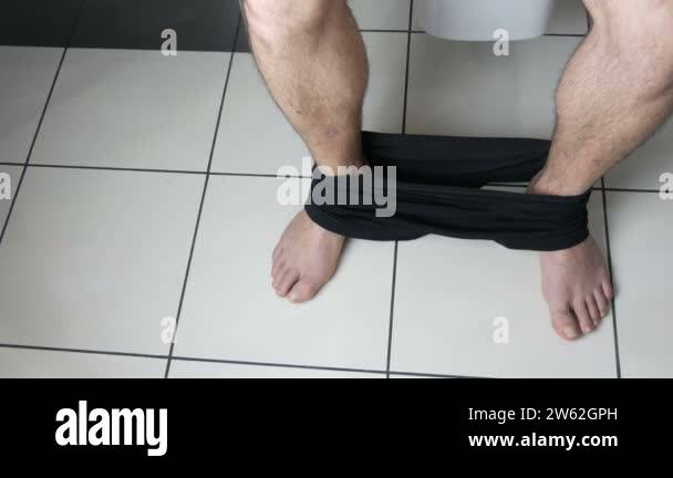 Legs of a man sitting on the toilet in the bathroom. Defecation process ...
