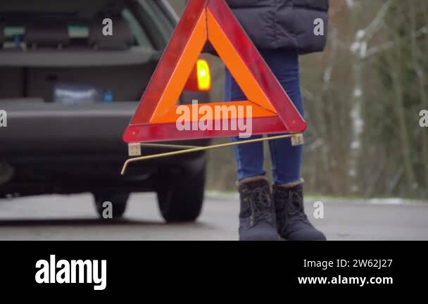 A woman sets up an emergency stop sign while standing by a wrecked car ...