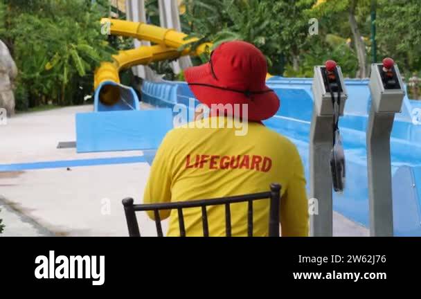 Back view of a male lifeguard in uniform at a water park sitting on a ...