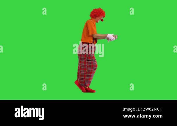 A happy male clown holding a present and walking on a Green Screen ...