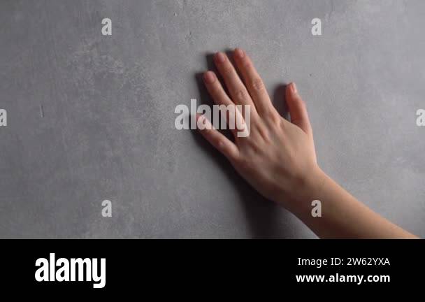 Woman hand palm is touching grey concrete plaster painted hall wall ...