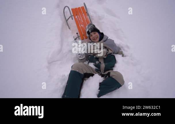 Teenager boy fell into the snow from a sled and waves his hand. Concept ...