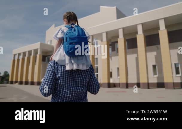 Dad carries on his shoulders little kid with backpack to school, girl ...