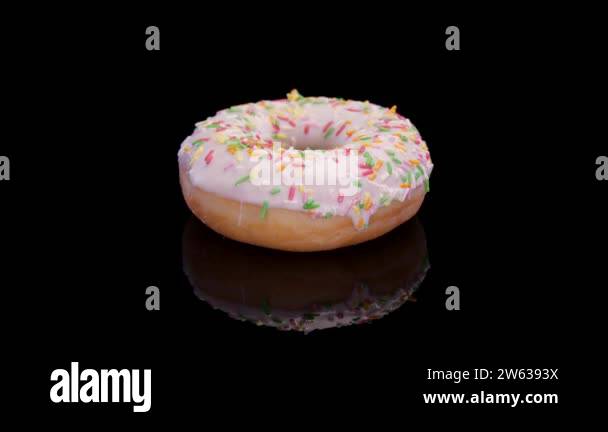 Donut with icing and colorful sprinkle rotating on a black background ...