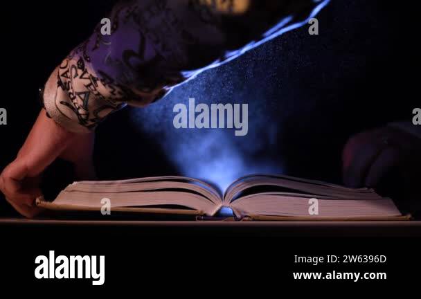 An open book lies on a table in a dark studio under the spotlight. The ...