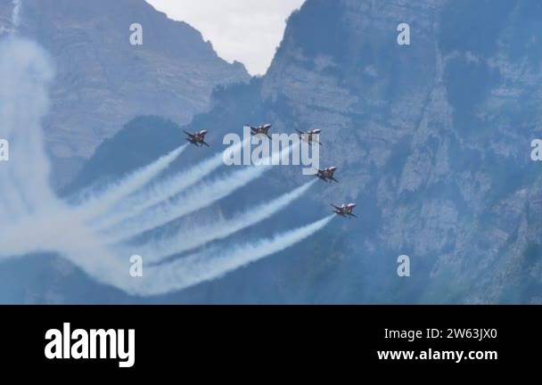 Military plane passes under an arrow formation of 5 jets with white ...