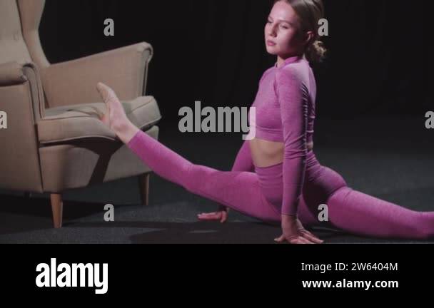 Young female gymnast sits on splits throwing her leg on a chair and ...
