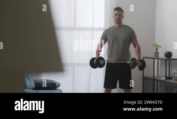 bodybuilder is training at home, lifting dumbbells, training muscles of ...