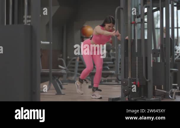 A young woman lifts her leg in a crossover to train her thigh and leg ...