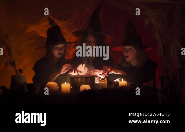 Three young girls dressed in witch's attire are conjuring over the ...