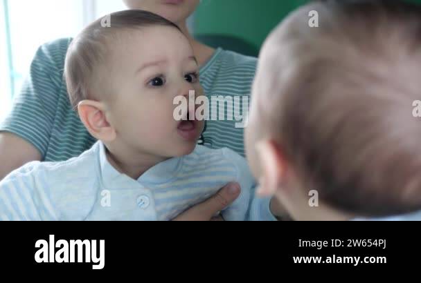 A cute seven-month-old newborn baby plays with a mirror at home with ...