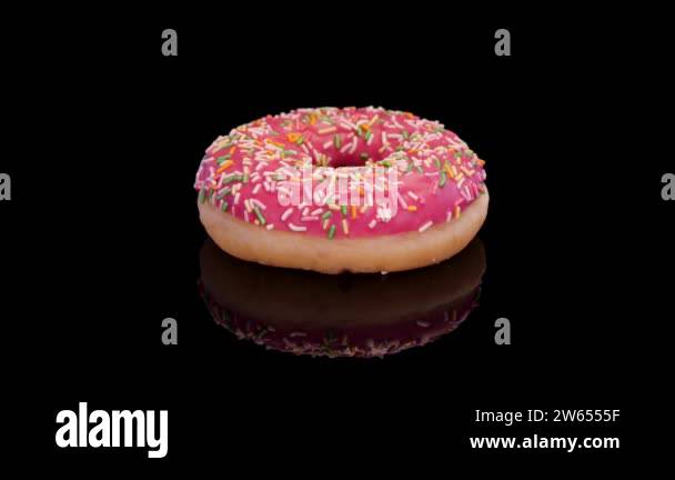 Donut with pink icing and colorful sprinkle rotating on a black ...