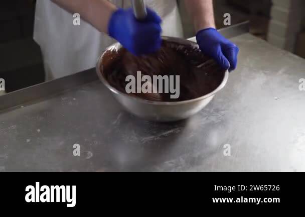 A pastry chef stirring melted dark chocolate in a bowl, close-up ...
