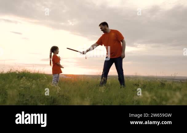 Daughter and dad play with toy swords in their hands on the field ...