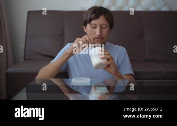 A man is eating yogurt from a white plastic can. Camera moves and ...