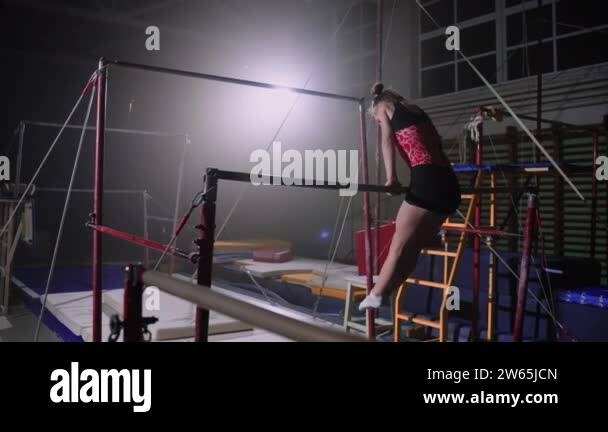 sporty female gymnast is performing exercises on uneven bars in ...