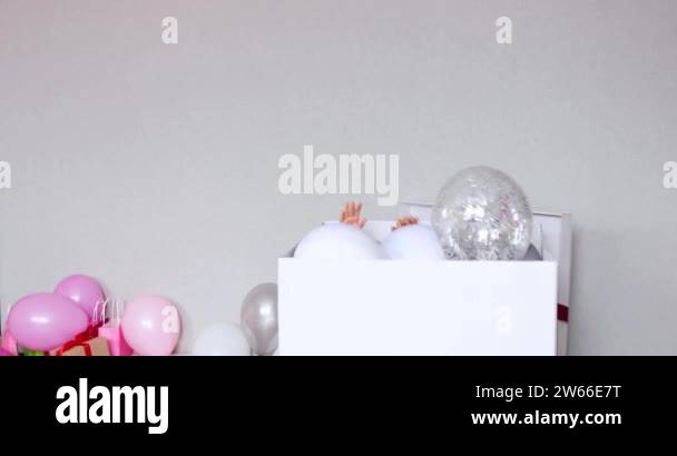 Cute, joyful little girl in pink dress jump out of the big present gift ...