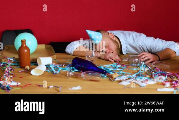 Bearded man sleeping at table in messy room in blue cap after bachelor ...