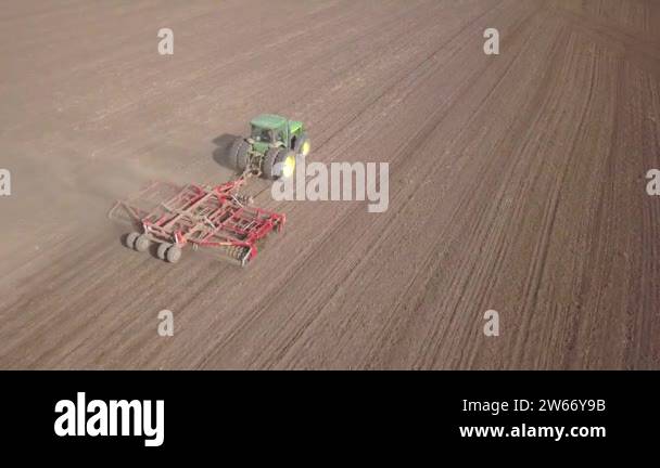 Top down aerial view of green tractor cultivating ground and seeding a ...