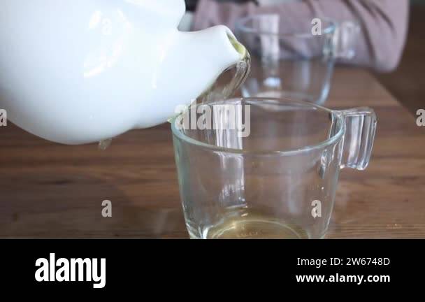 Woman holding a ceramic tea pot spilling clear green tea while trying ...