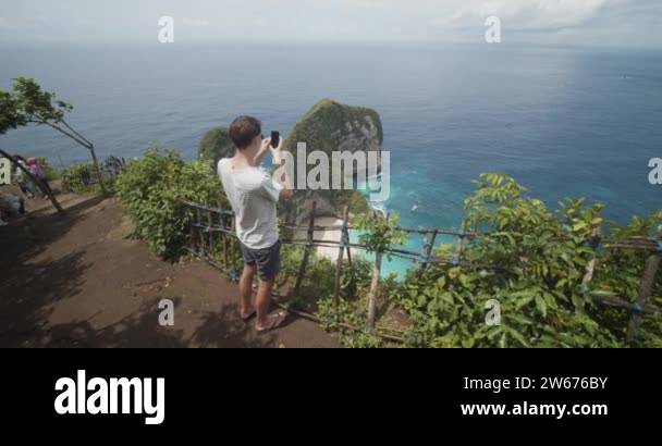 Back view of a male tourist taking pictures of the beautiful tropical T ...