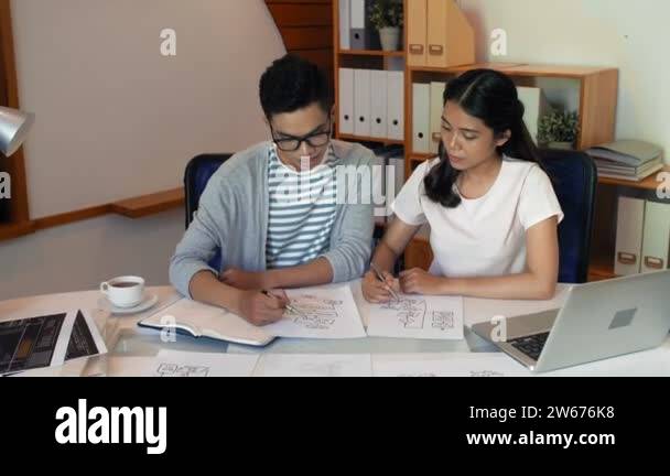 Young creative Asian man drawing project sketches and explaining ...