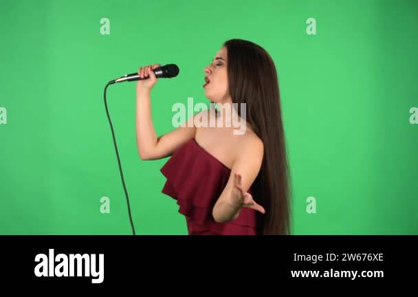 Portrait of beautiful young woman sings song into microphone and dances ...