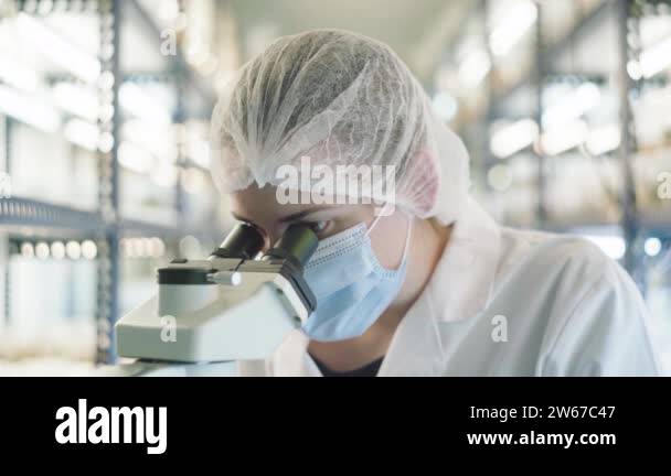 Focused female biologist examining chemical substance under microscope ...
