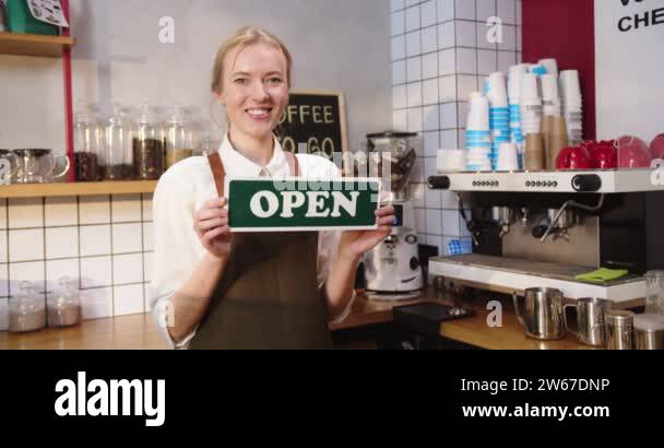 Joyful woman standing behind bar and showing OPEN sign in new ...