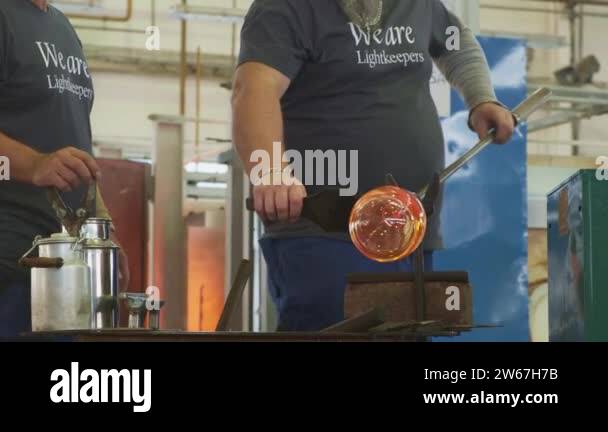 Glass blower shaping a bubble of melted glass on a rod. Glass ...