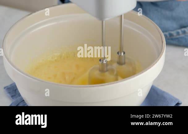 Close-up mixing egg whites, yolks and sugar in a ceramic bowl with a ...