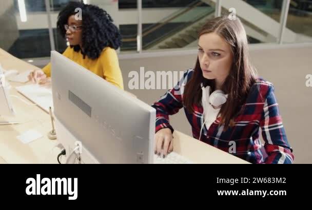 Two girls are sitting in computer room at university and working on ...