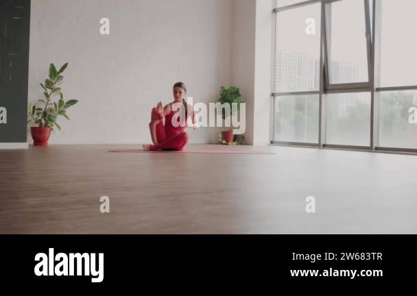 Young woman in red sports uniform performs the Astavakrasana asana in ...