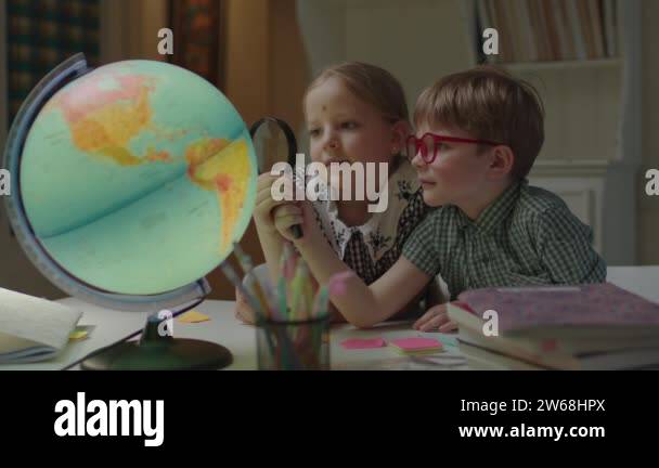 Two kids studying Earth globe with magnifying glass. Siblings learning ...