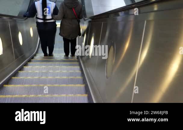 Rear view of two unidentified women going down by escalator at subway ...