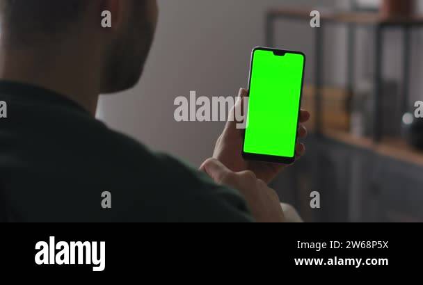 male user is using modern app, swiping and tapping on screen of smartphone, green screen ...
