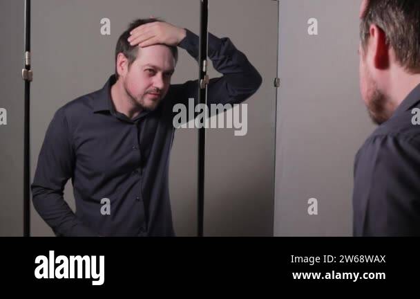 A 35-year-old young man looks in the mirror and touches his hair ...