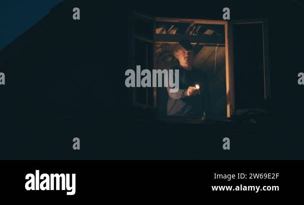 Man in cowboy hat in attic of house. He gives signal with candle from ...