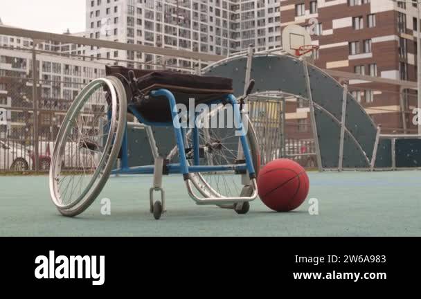 Low-angle locked-down of wheelchair on outdoor basketball court, ball ...