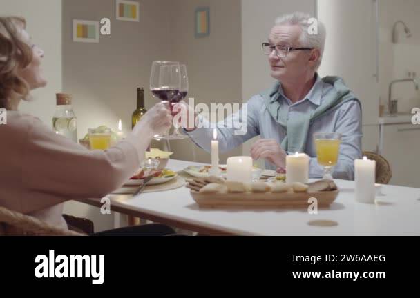 Senior man giving a toast, clinking glasses and drinking red wine while ...