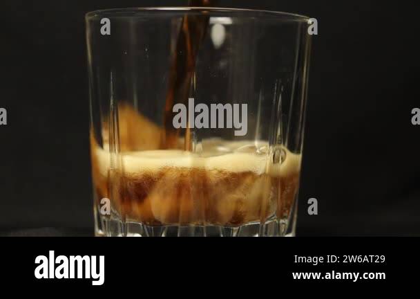 The process of pouring a carbonated cola soft drink into a glass beaker with ice cubes Stock ...