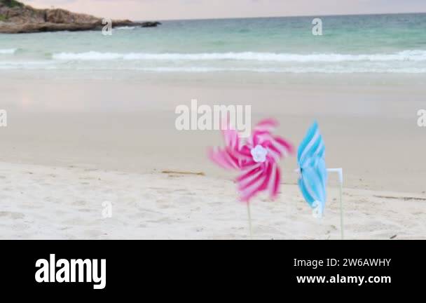 Pink and blue pinwheels toy spinning on white sand beach, two colorful ...